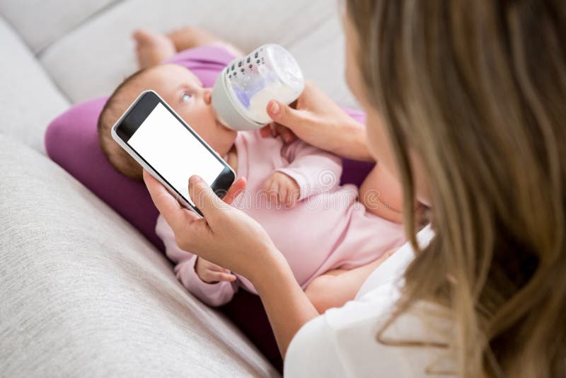 Mother Using Mobile Phone while Feeding Her Baby with Milk Bottle Stock ...