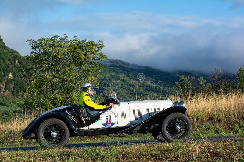 The Motorcycle is Driving by a Classic Car on the Side of the Road ...