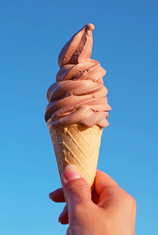 Chocolate Soft Serve Ice Cream Cone in Hand Against Blue Sunny Sky ... Chocolate Soft Serve Ice Cream Cone in Hand Against Blue Sunny Sky ...