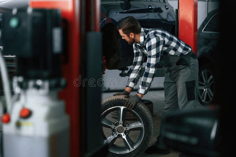 Moving the New Tire for a Car. Man in Uniform is Working in the Auto ...
