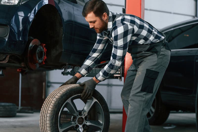 Moving the New Tire for a Car. Man in Uniform is Working in the Auto ...