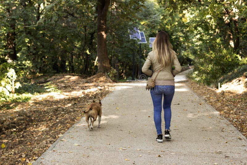 Mulher Caminhando Em Uma Pista De Parque Com Um Cachorro No Outono ... Mulher Caminhando Em Uma Pista De Parque Com Um Cachorro No Outono ...