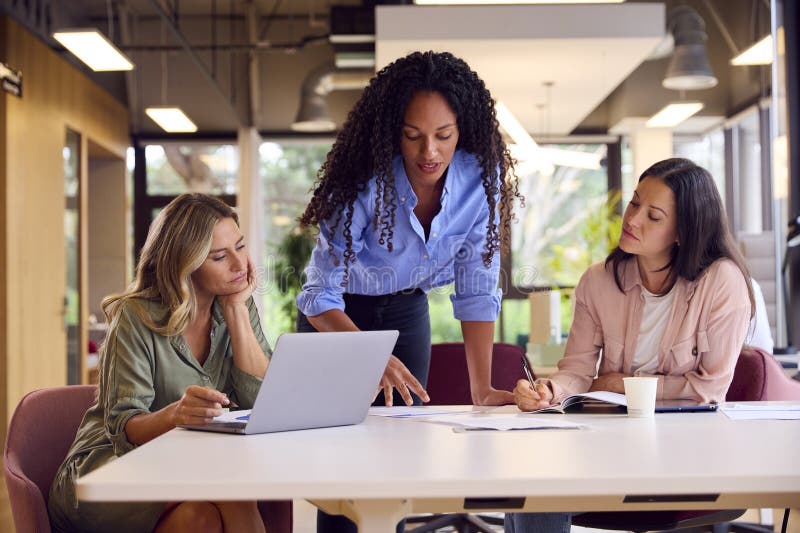 Multi-Cultural Female Business Team Sitting at Desk in Open Plan Office ...