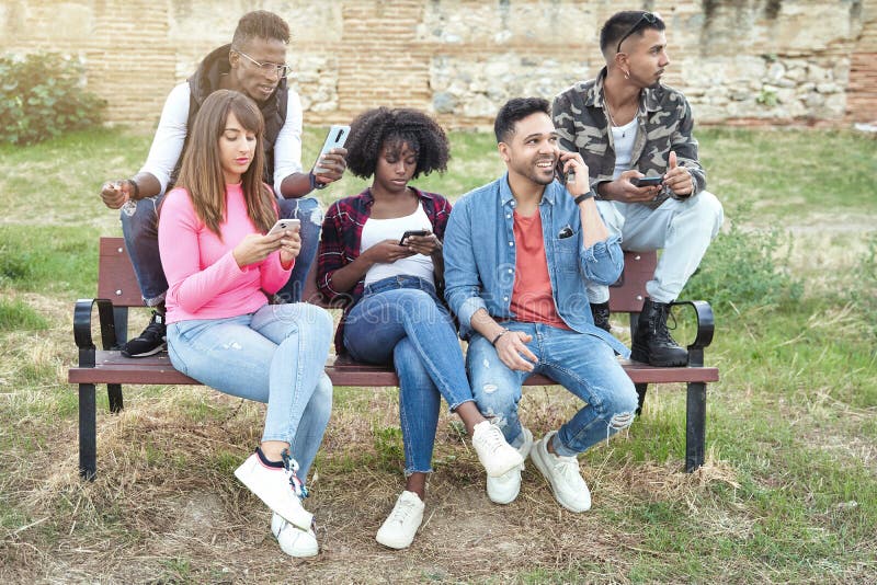 Multi Ethnic Friends Using Their Mobile Phones While Sitting On A Bench