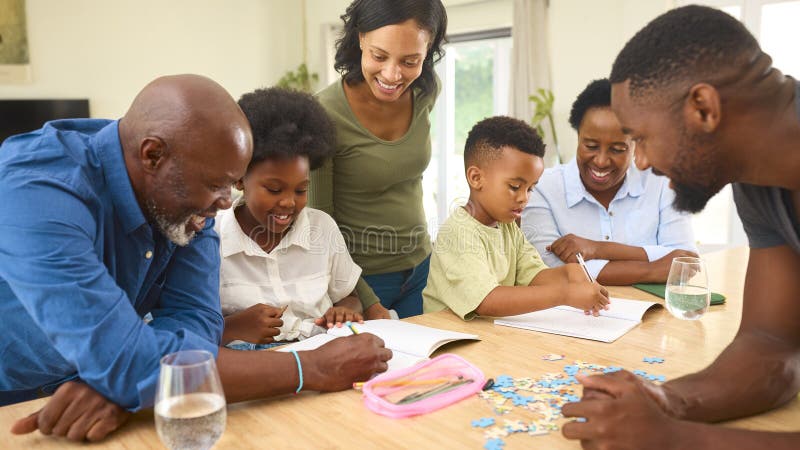 Multi-Generation Family Helping Children with Homework Sitting at Table ...