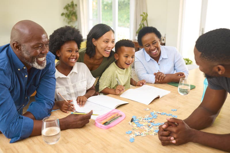 Multi-Generation Family Helping Children with Homework Sitting at Table ...