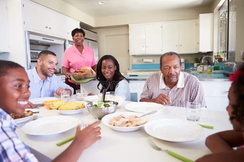 Multi-Generation Family Sitting Around Table Eating Meal Stock Image ...