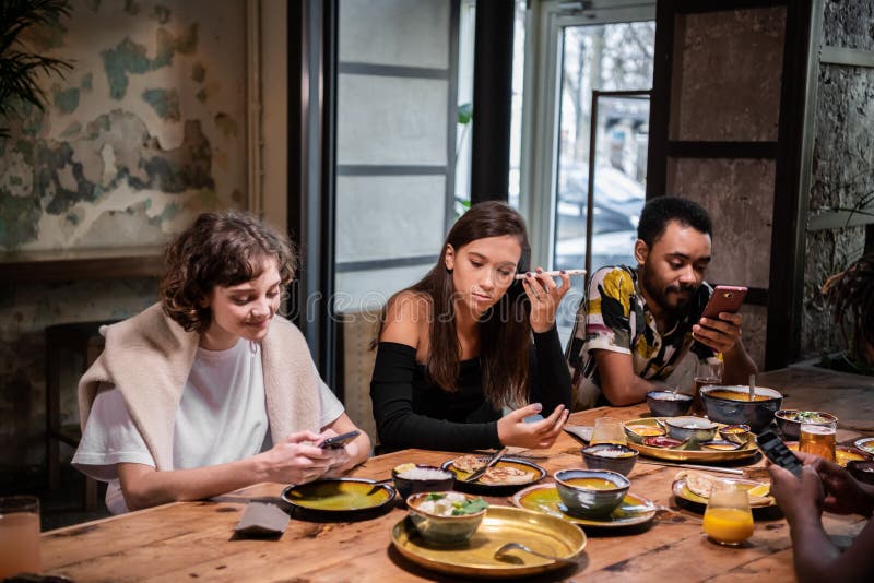 A Multicultural Group of Students Sharing Food in a Cafe and Usi Stock ...