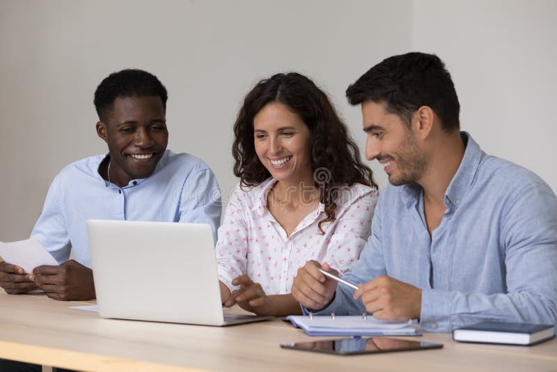 Multiethnic Colleagues Sit at Desk Using Laptop Engaged in Teamwork ...