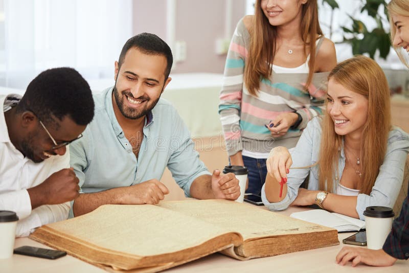 Multiethnic Young People Sitting at Table Reading Reference Books for ...