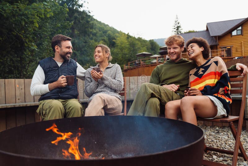 Multinational People Drinking Tea and Smiling Around Campfire in Forest ...
