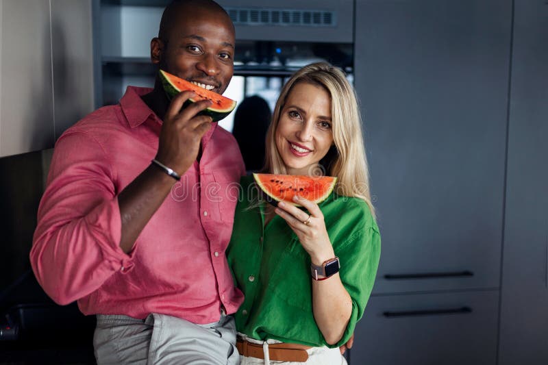 Multiracial Couple Eating Melon in Kitchen during Hot Sunny Days. Stock ...
