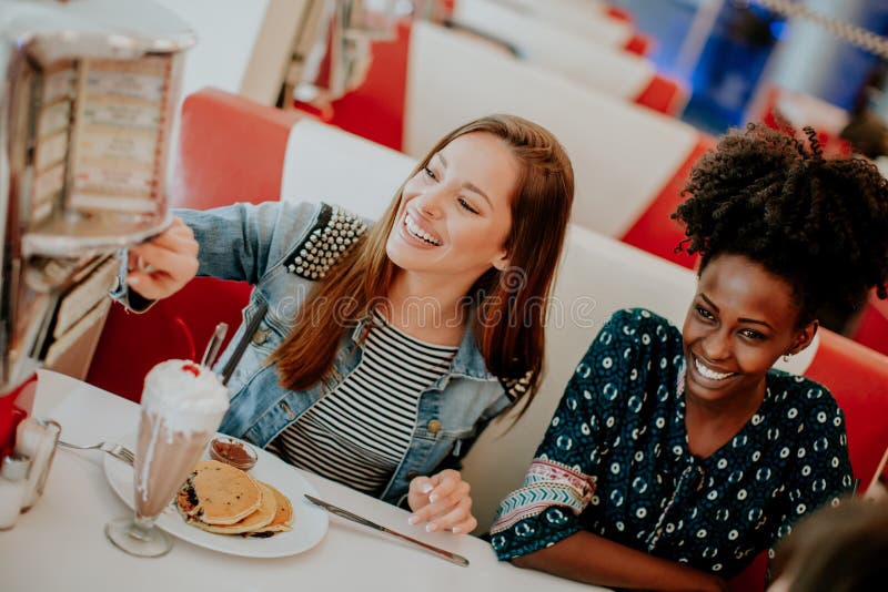 Multiracial Female Friends Eating Fast Food At A Table In The Di Stock