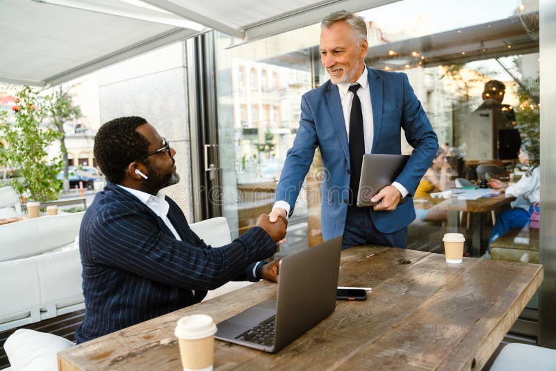 Multiracial Men Handshaking while Working with Laptops in Cafe Stock ...