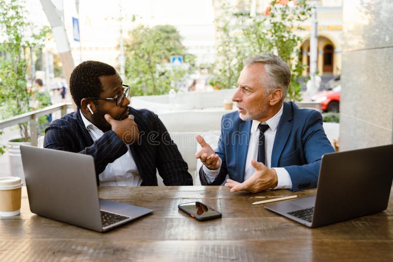 Multiracial Men Talking and Gesturing while Working with Laptops in ...