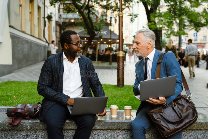 Multiracial Men Talking while Working with Laptops and Drinking Coffee ...