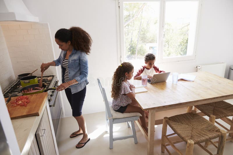 Mum Cooking while Kids Work at Kitchen Table, Elevated View Stock Image ...