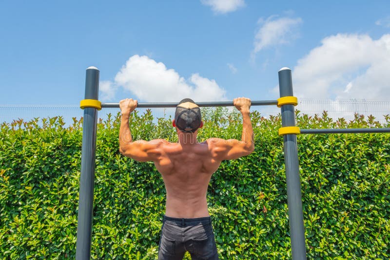 Muscular Caucasian Man in a Cap Doing Pull-ups on the Horizontal Bar in ...