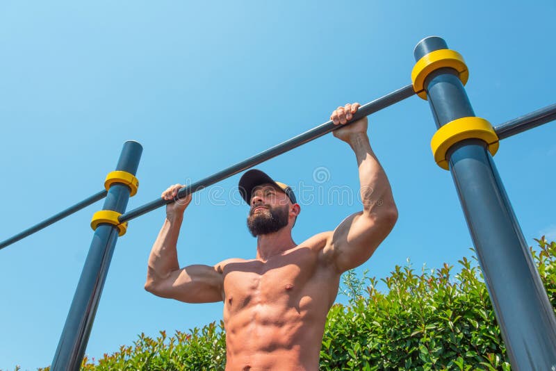 Muscular Man in a Cap Doing Pull-ups on the Horizontal Bar with His ...