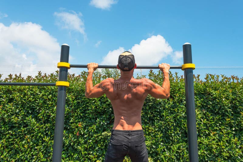 Muscular Man in a Cap Doing Pull-ups on the Horizontal Bar in the Park ...