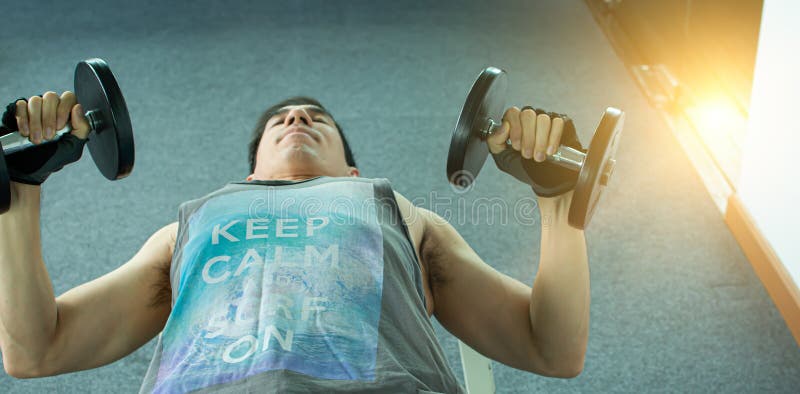 A Muscular Man is Doing Exercising by Lifting Dumbbells in Gym Stock ...
