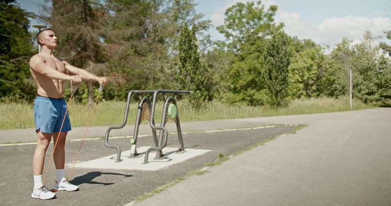 Muscular Man Performing Front Raises with Resistance Bands in a Park ...