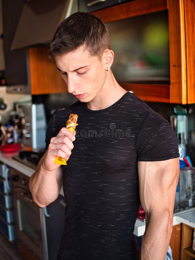 Muscular Young Man Eating Cereal Bar, Looking at Camera Standing, Stock ...