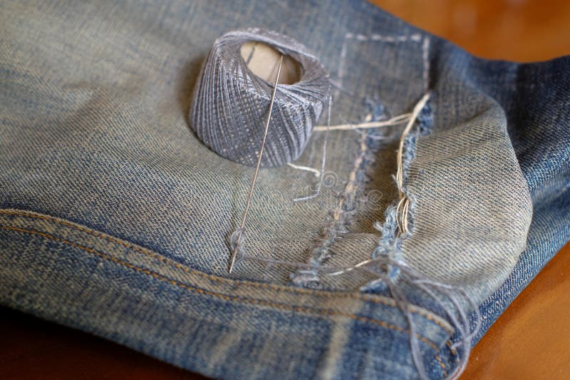 A Needle and Thread Sew Up a Hole in a Denim. Work of a Seamstress or ...