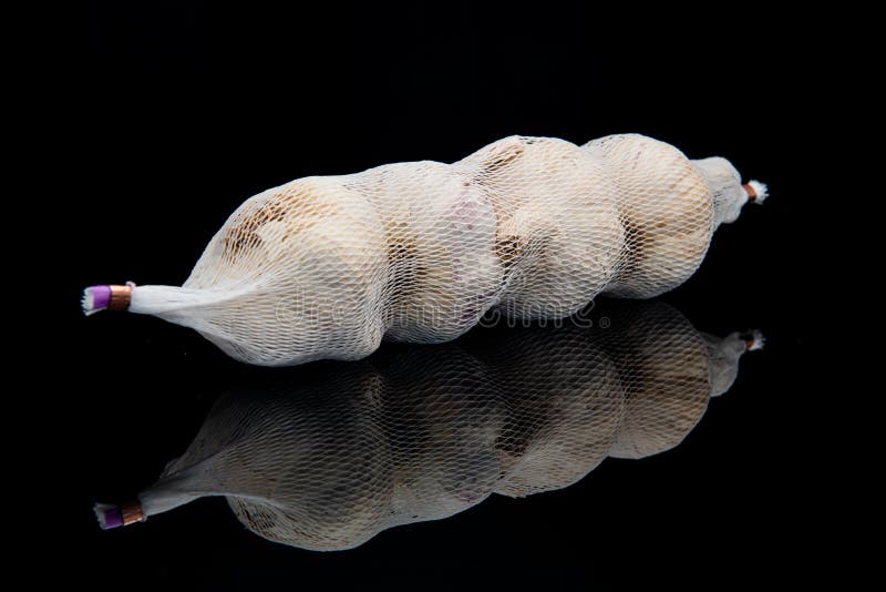 A Net of Four Garlic Bulbs Isolated Against a Black Background ...