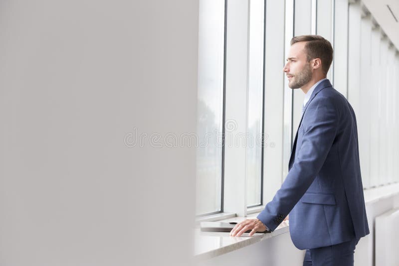 Thoughtful Handsome Young Businessman Looking through Window in New ... Thoughtful Handsome Young Businessman Looking through Window in New ...