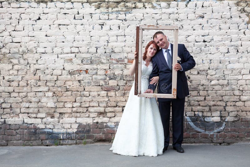 Newlywed Couple Holding Portrait Frame, Brick Wall Stock Photo - Image ...