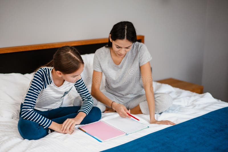 Nice Beautiful Mother and Daughter Doing Homework while Sitting on Bed ...
