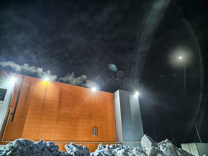 Night View of an Industrial Building with Bright Lights Against a ...