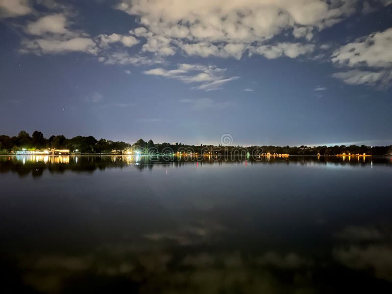 Night View of a Lake in Which the Clouds and Lights on the Shore are ...