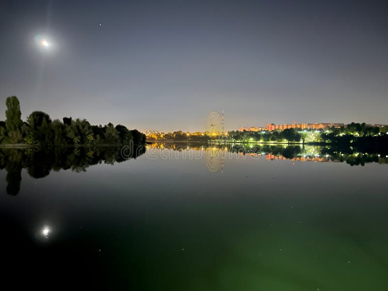 Night View of Trees, Moon and City Reflecting on the Lake Water Stock ...