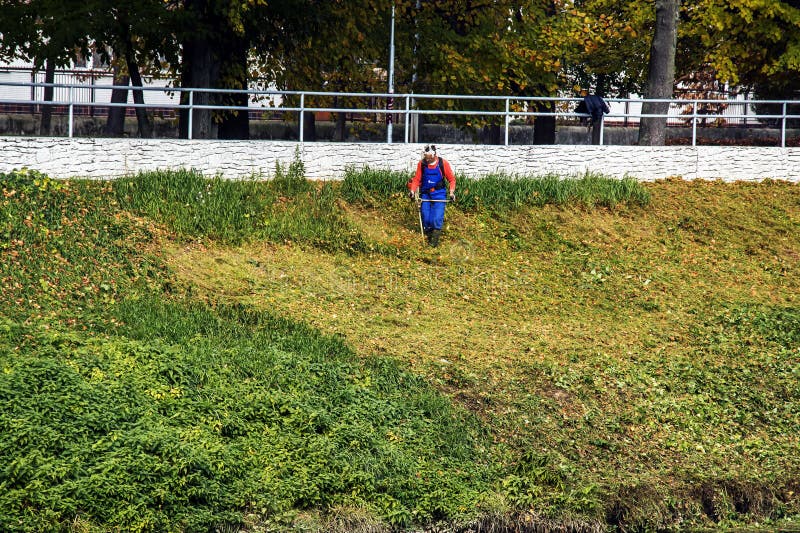 A Municipal Worker Cuts the Grass Using Power Tool String Lawn Trimmer ...