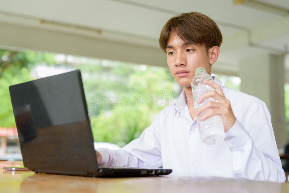 Non Binary University Student Sitting in College Campus Using Laptop Computer and Drinking Water ...