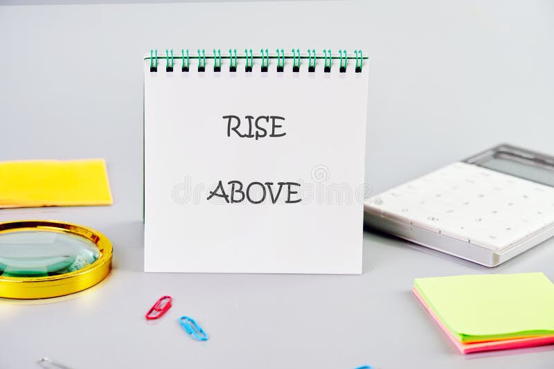 A Notepad Displaying the Phrase RISE ABOVE Sits on a Desk with Various ...