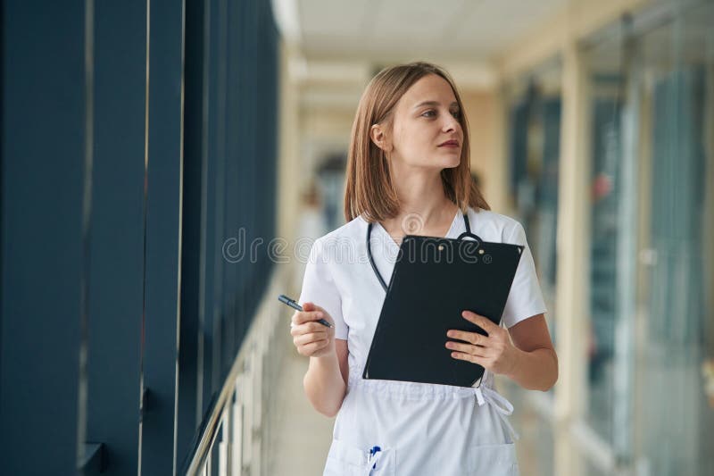 With Notepad in Hands. Female Doctor in White Coat is in the Hall Stock ...