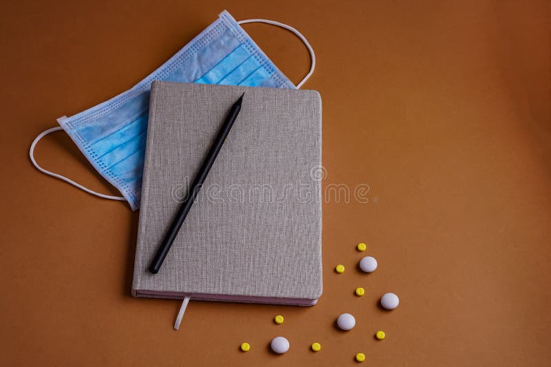 Notebook and Pills and a Protective Mask and Pencil on a Brown ...