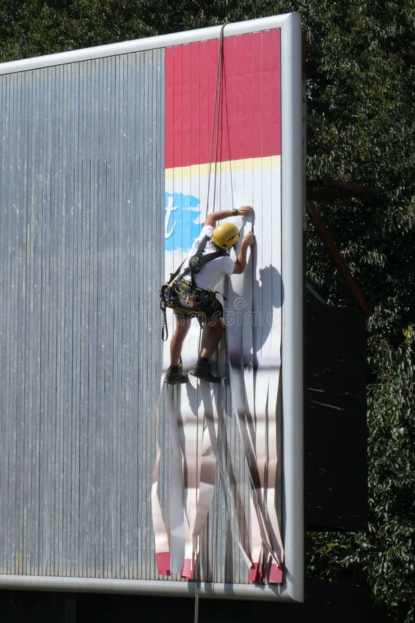 A Worker Hung on a Rope Changes an Advertisement on a Billboard ...
