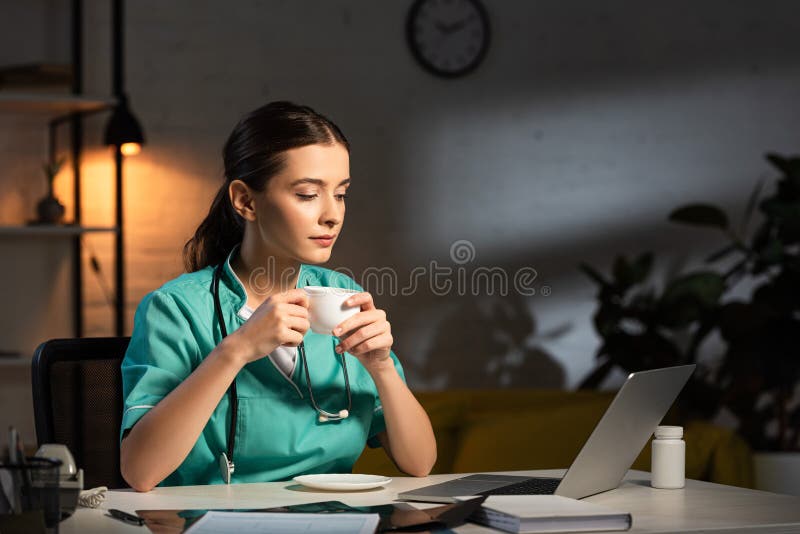 Nurse in Uniform Sitting at Table and Holding Cup during Night Shift ...