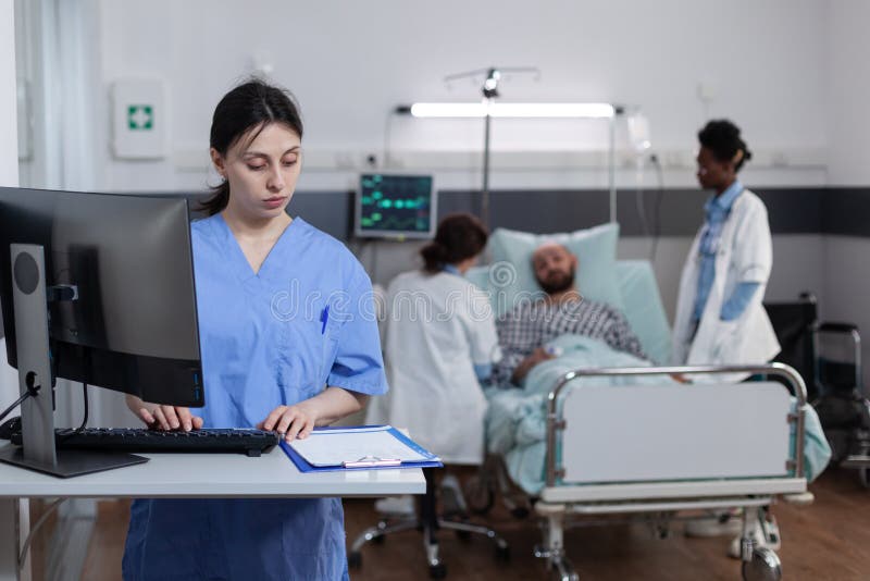 Nurse Using Personal Computer To Complete Patient Admission Chart while ...