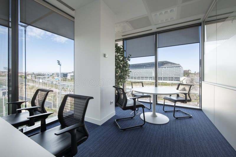 An Office with Large Windows with a Small White Conference Table and ...