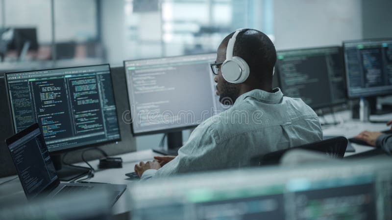 Office: Professional Black it Programmer Uses Headphones while Working ... Office: Professional Black it Programmer Uses Headphones while Working ...