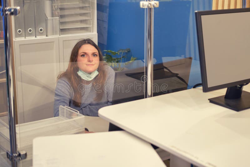 Office Worker in Face Mask at Computer in a Room with Protective Glass ...