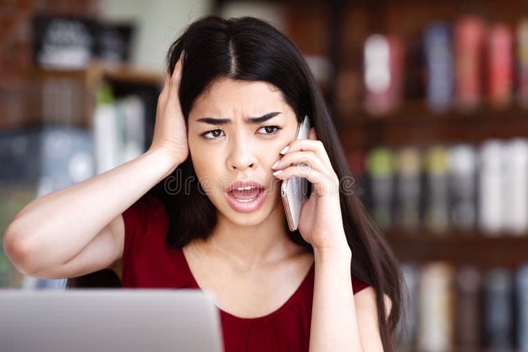 Frustrated Asian Woman Having Computer Problems, Talking on Cellphone ...