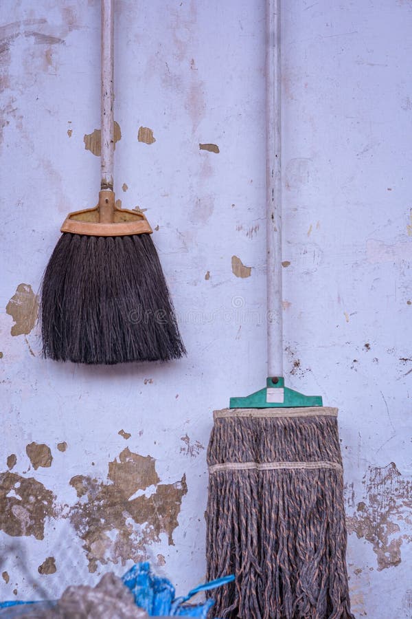 An Old Broom and Mop Hang on a Worn, Peeling White Wall, Showcasing ...