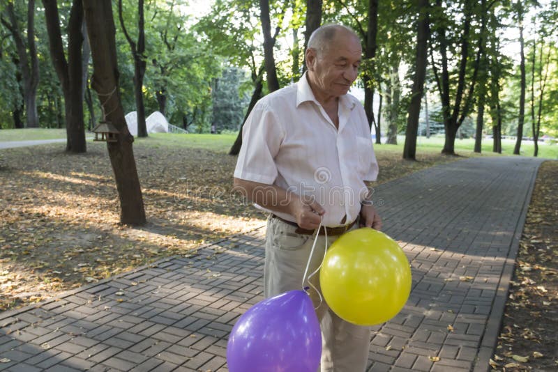 An Old Man is Playing in the Park with Bright, Balloons on His Birthday ...
