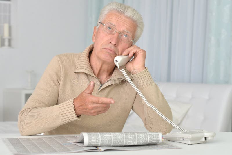 Old Man Reading Newspaper and Talking on Phone at Home Stock Photo ...